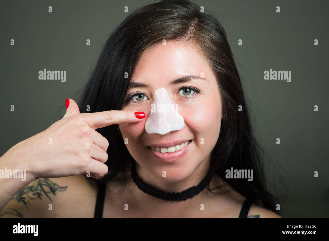 Beautiful young woman pointing in from of her nose an open white nose ...