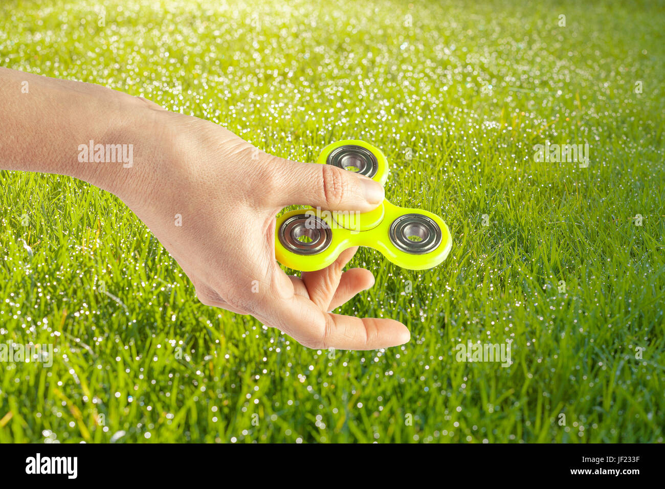 Female hand holding yellow fidget spinner on a grassy sunny background ...