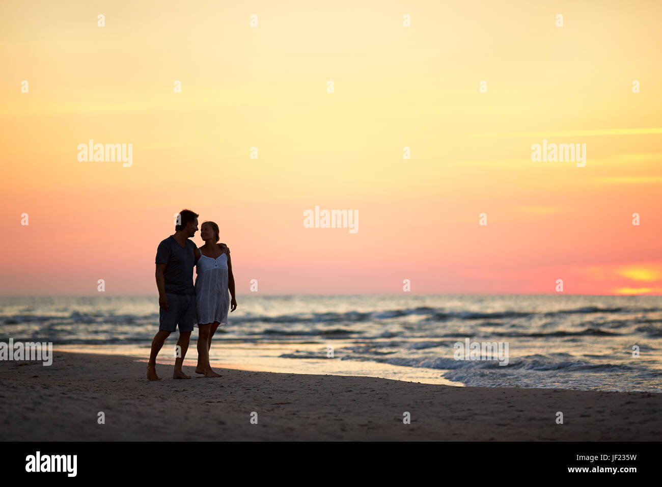 Couple on beach at sunset Stock Photo - Alamy