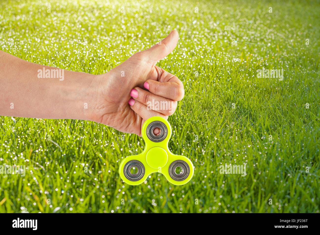 Female hand holding yellow fidget spinner with thumbs up on a grassy ...