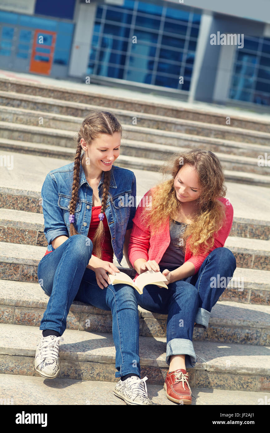 Two friends reading a book on the steps of the University. youth ...