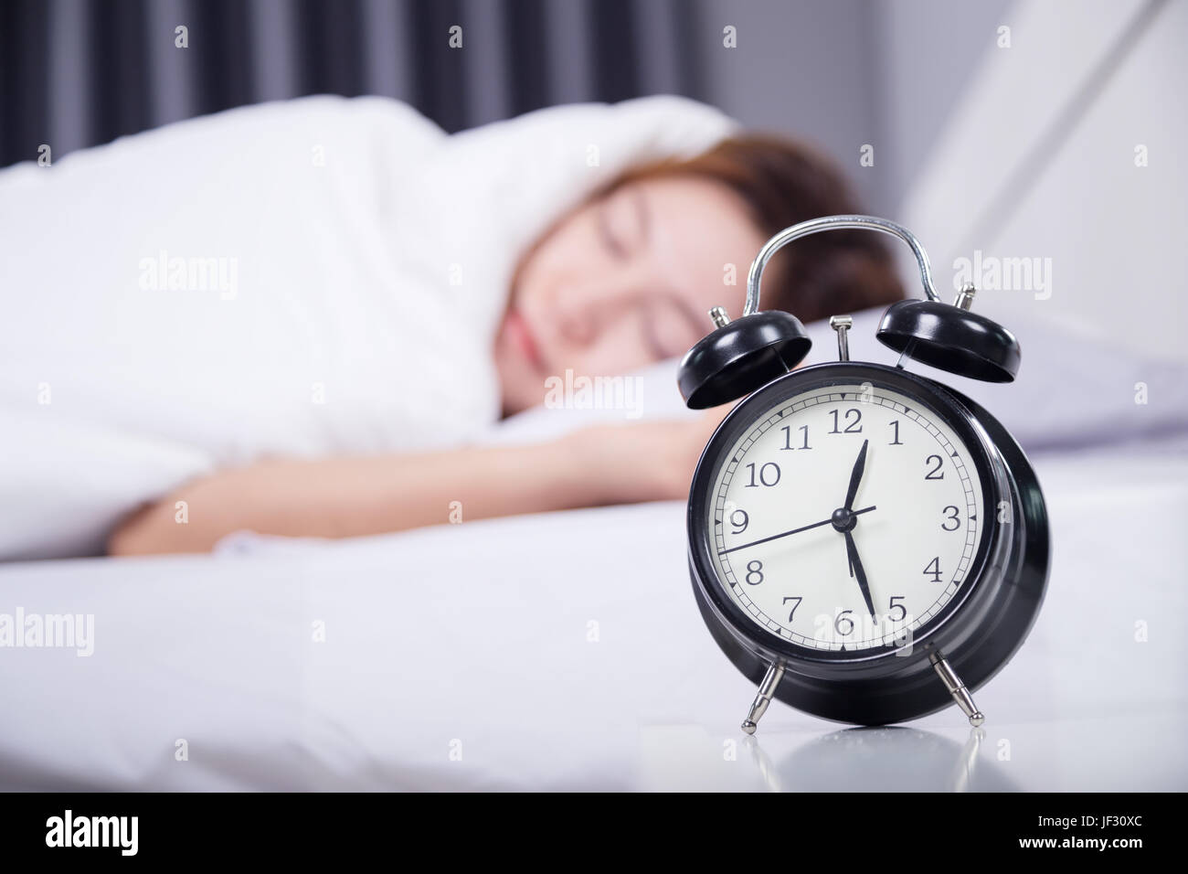 clock with woman sleeping under white blanket on the bed Stock Photo ...