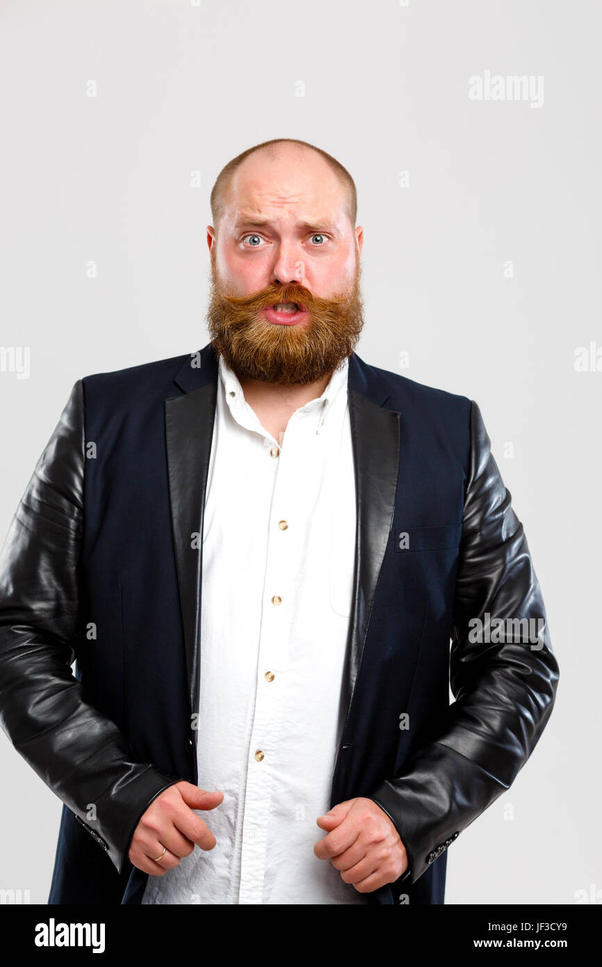 Frowning man with ginger beard in black jacket on empty gray background ...