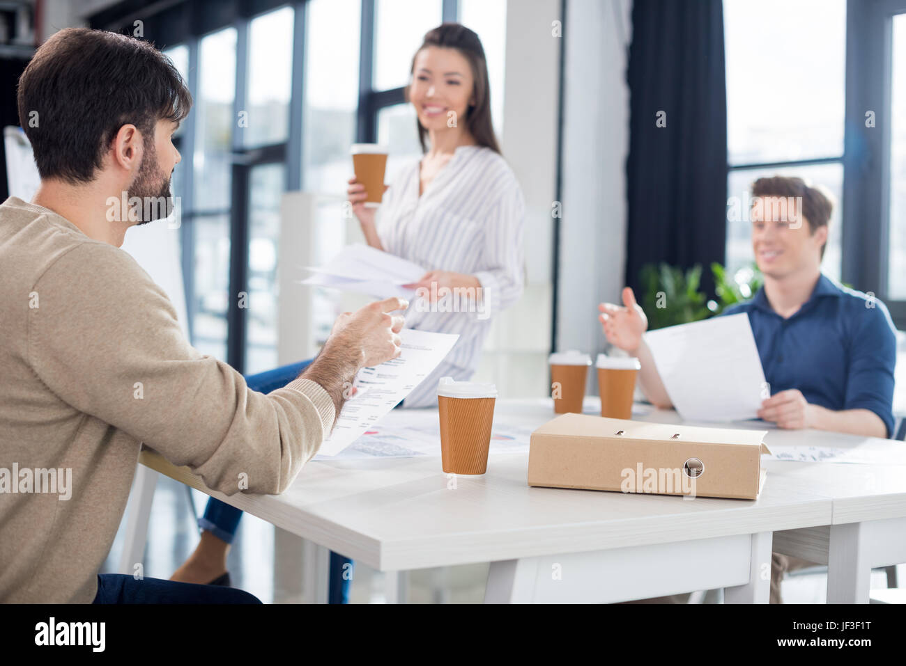 Professional young businesspeople drinking coffee from paper cups and ...
