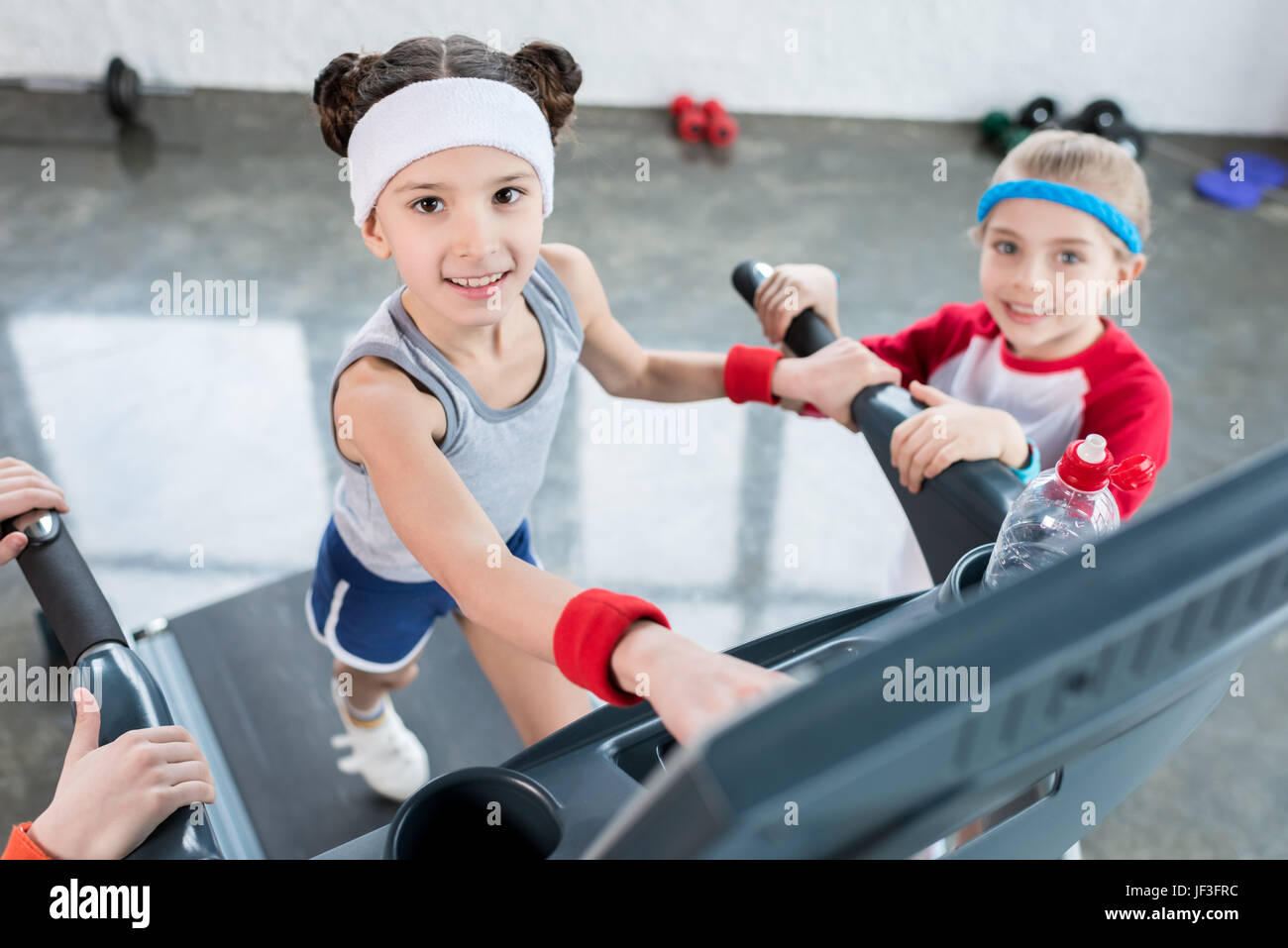 Adorable little girls in sportswear exercising on treadmill and smiling ...