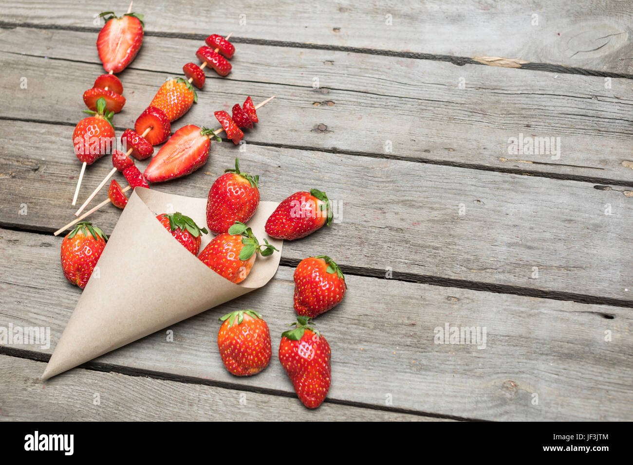 whole fresh red strawberries scattered of paper cone and sliced ...