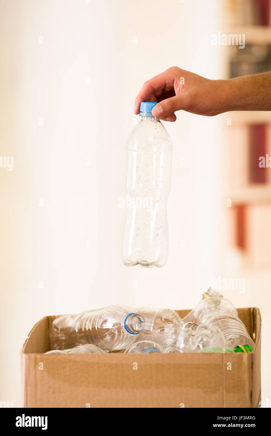 Close up of a hand putting a plastic bottle inside of a cardboard box ...