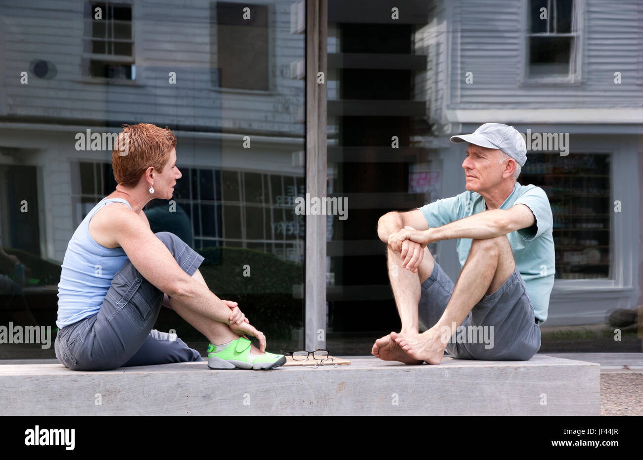 Two adults sitting and having a conversation while sitting on a ledge ...