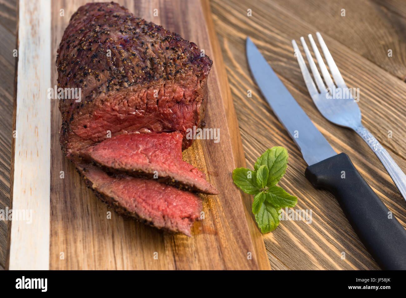 A large piece of grilled top sirloin sits on cutting board sliced and ...