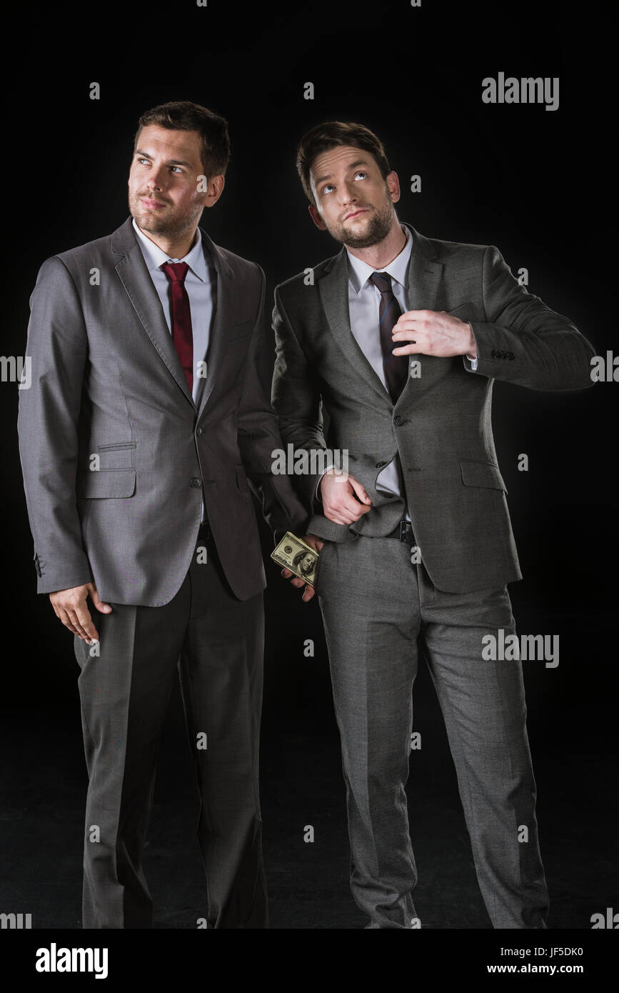 Businessman giving money and bribing business partner isolated on black ...