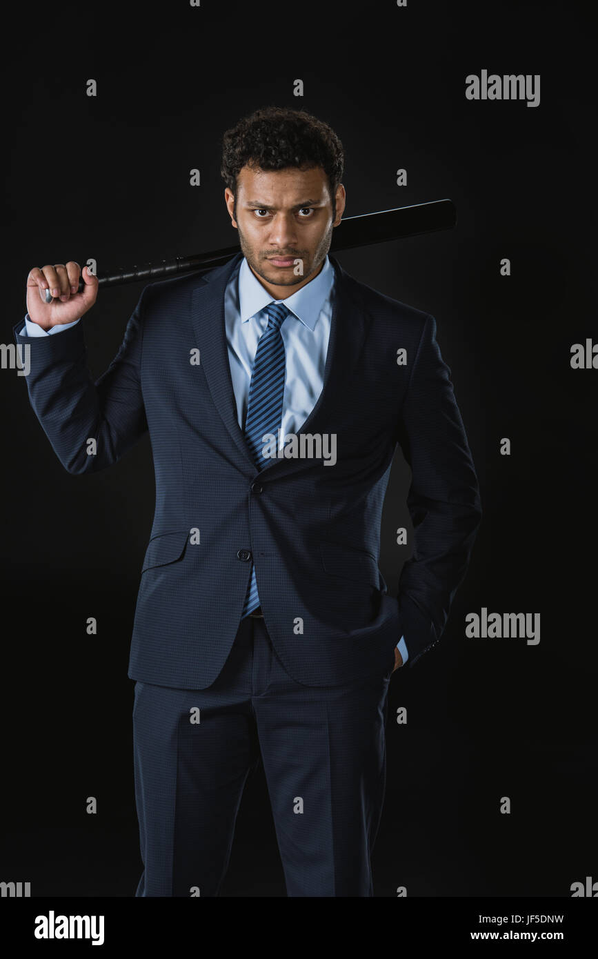 Confident young businessman with hand in pocket holding baseball bat ...