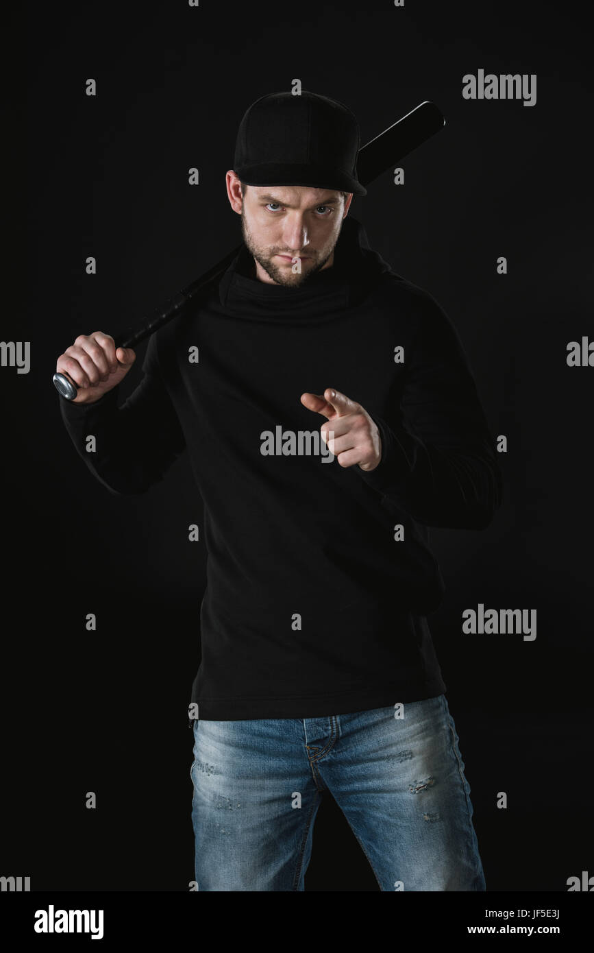 young robber in zoodie and cap with baseball bat isolated on black ...