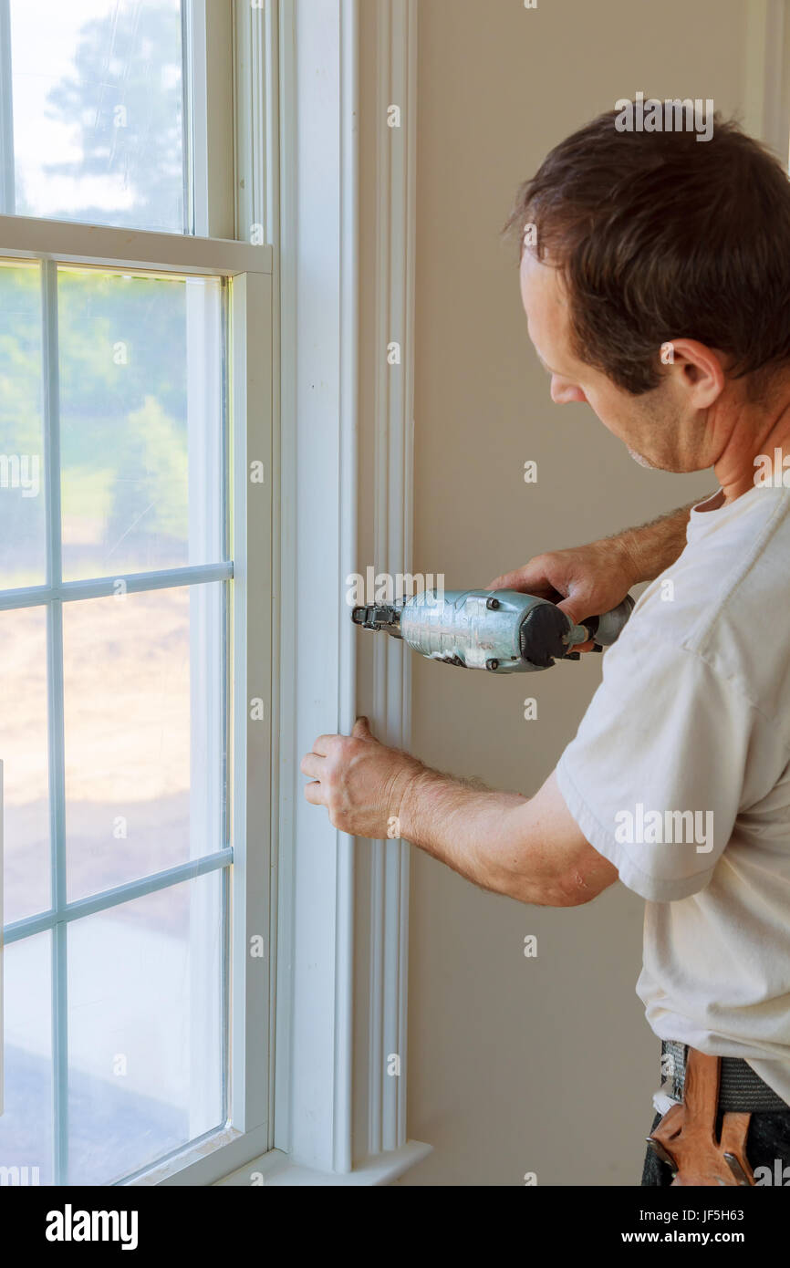 Carpenter brad using nail gun to moldings on windows, framing trim ...