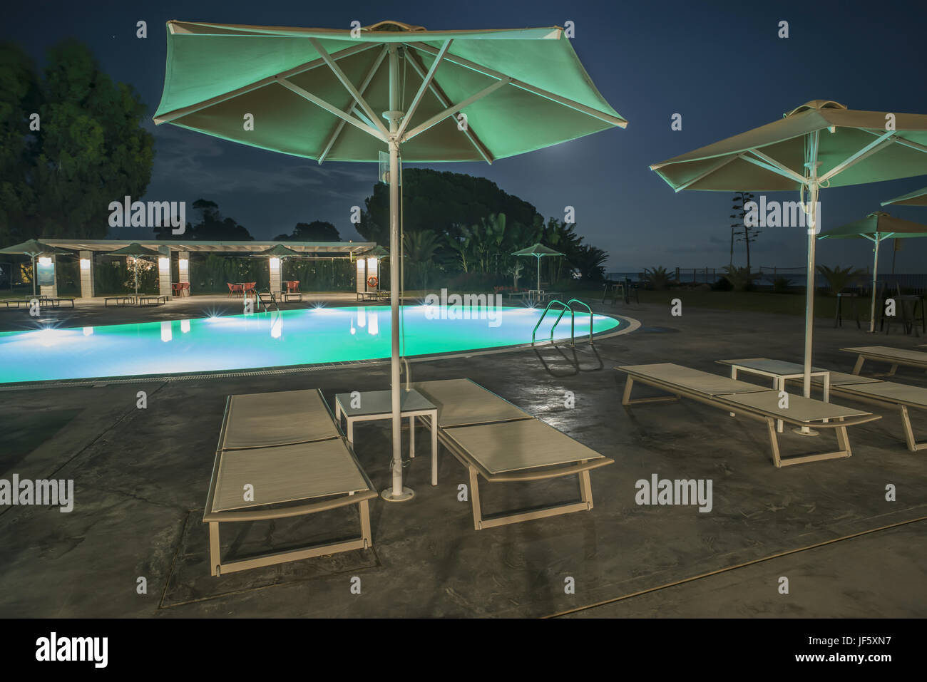 Pool, sunbeds and umbrellas at night Stock Photo - Alamy