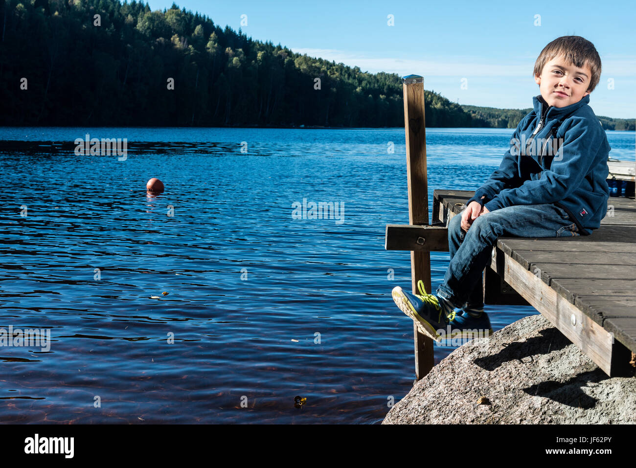 Boy sitting on jetty Stock Photo - Alamy