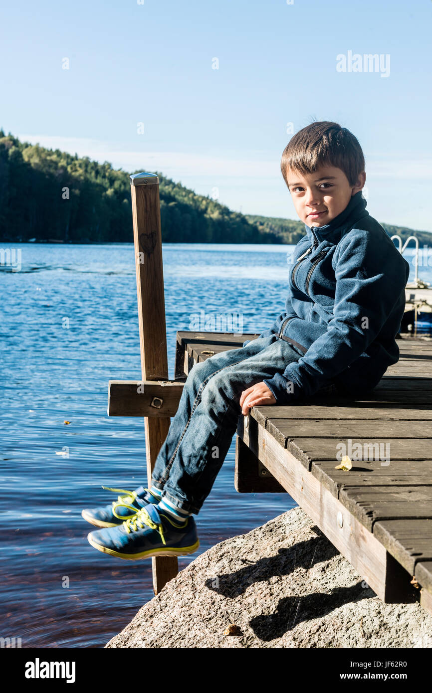 Boy sitting on jetty Stock Photo - Alamy