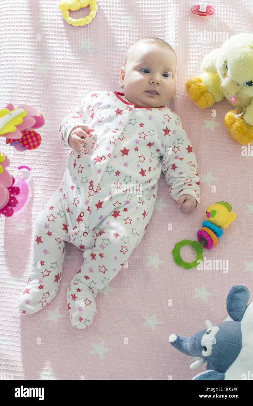 Baby girl in a bed with toys around Stock Photo - Alamy