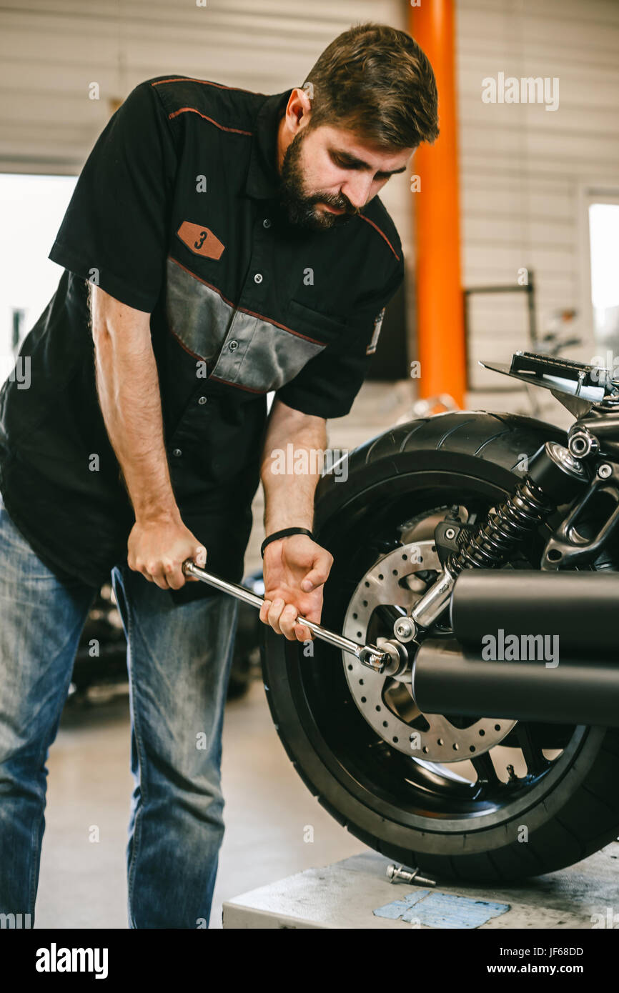 Handsome mechanic removing motorcycle wheel with special tools ...