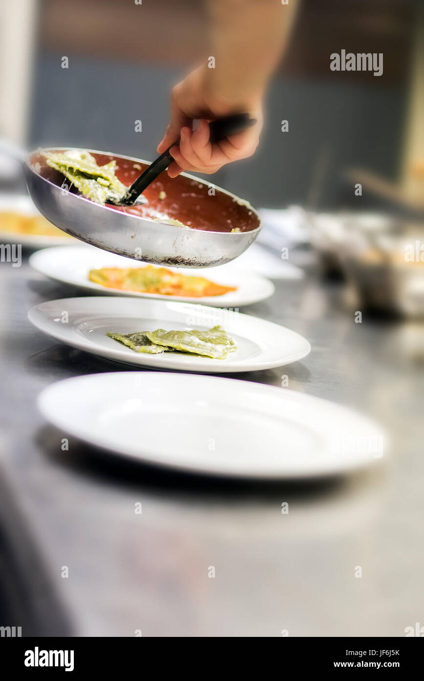 Chef serving cooked food in a restaurant kitchen spooning the ravioli ...