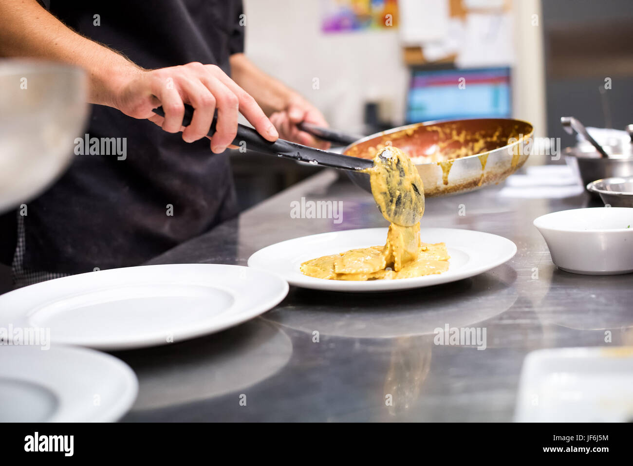 Chef serving Italian pasta in a restaurant kitchen spooning the cooked ...