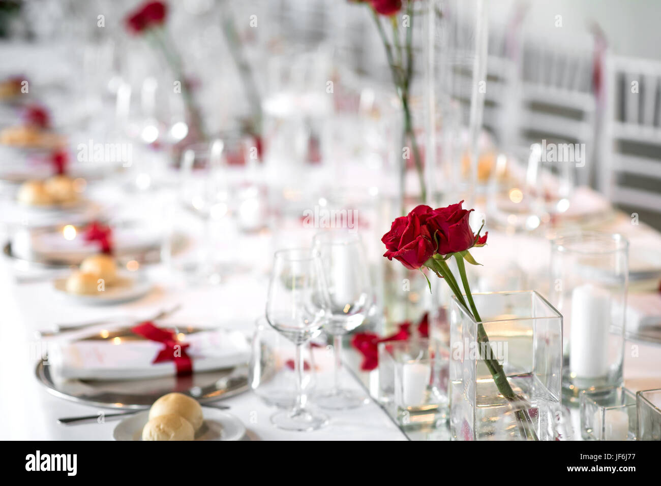 Stylish formal dinner table setting with red roses, serviettes tied ...