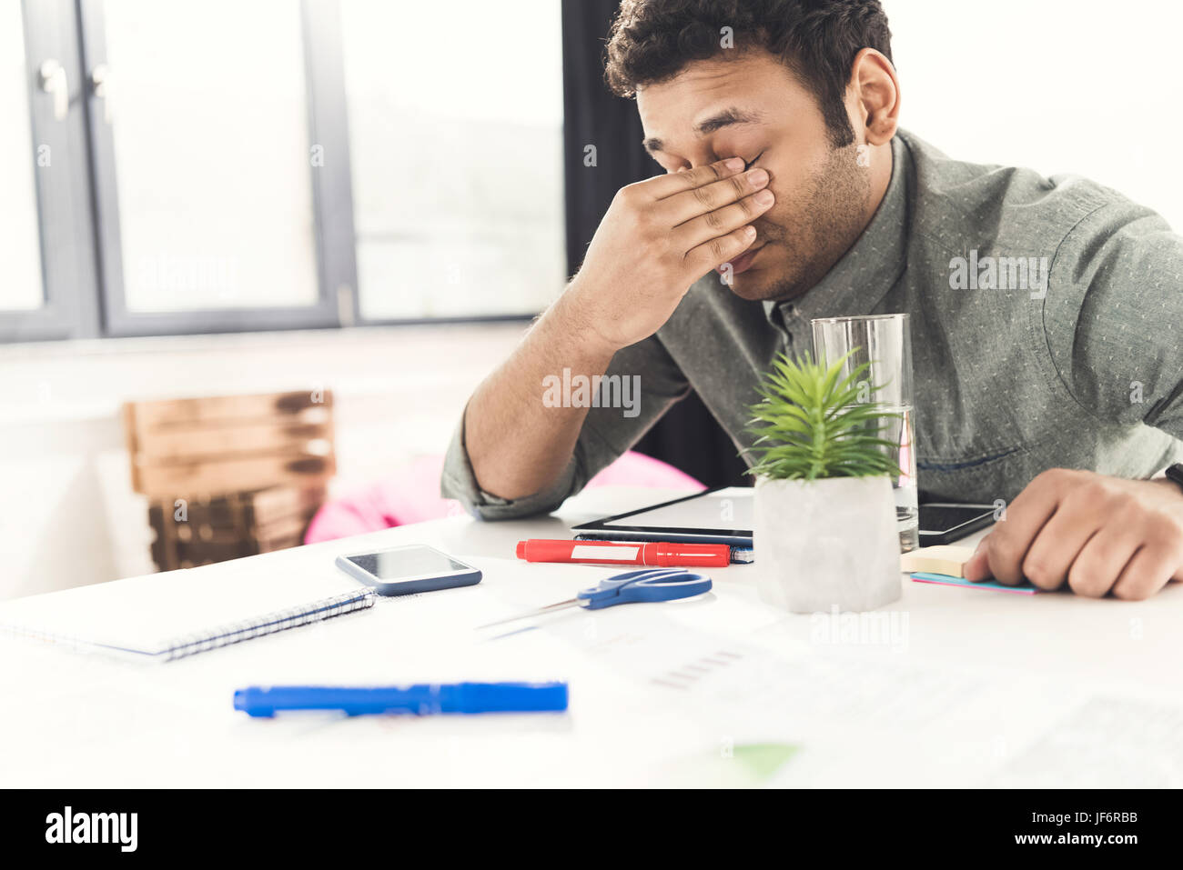 young tired casual businessman sitting at table in office, business ...