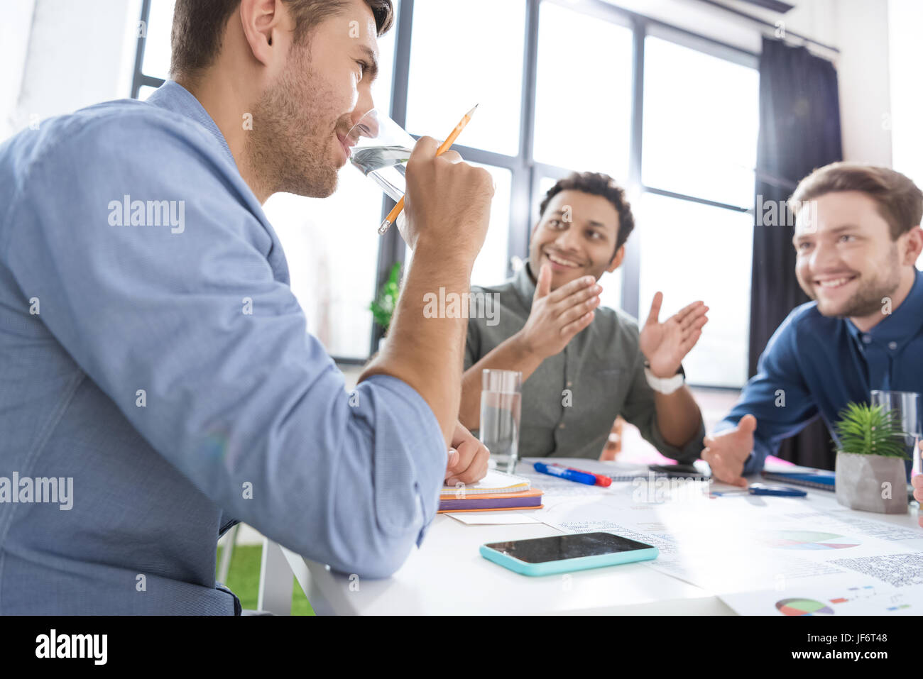 Smiling young businessmen drinking water and discussing new project ...