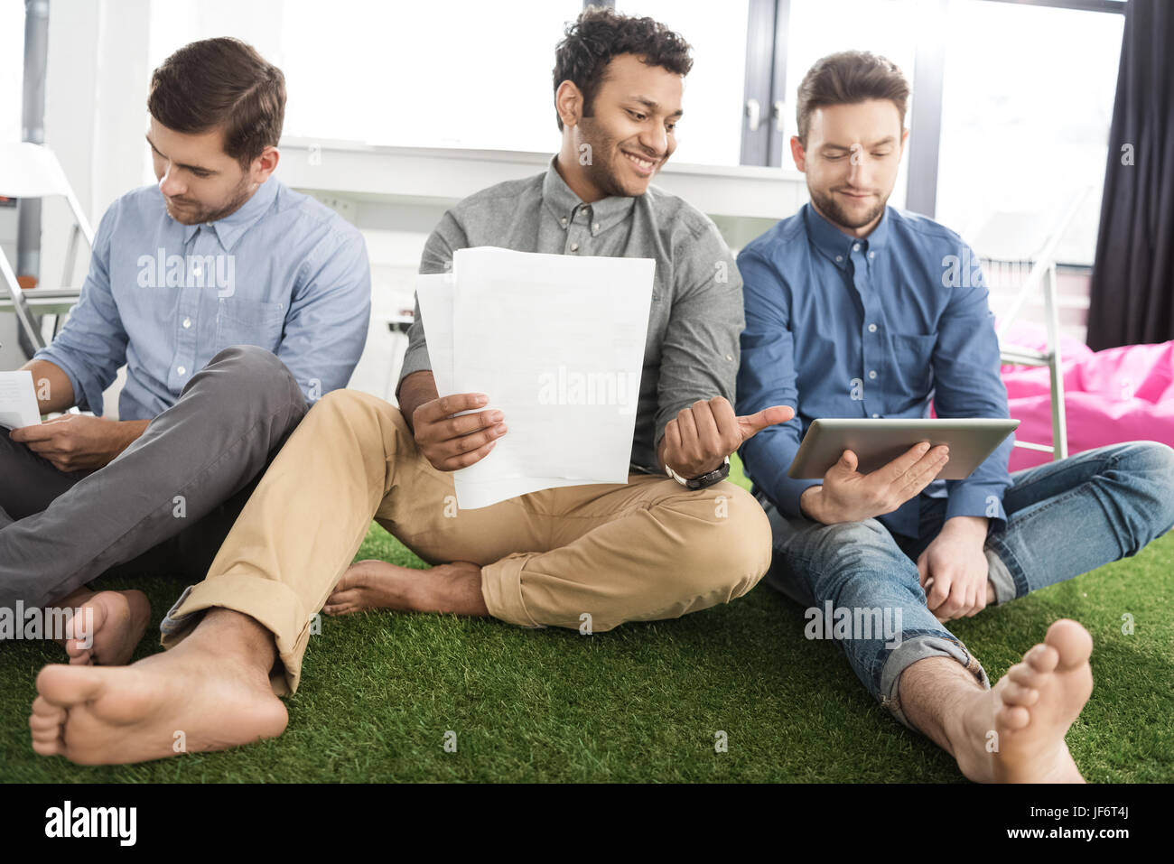 Smiling young barefoot businessmen sitting with papers and using ...