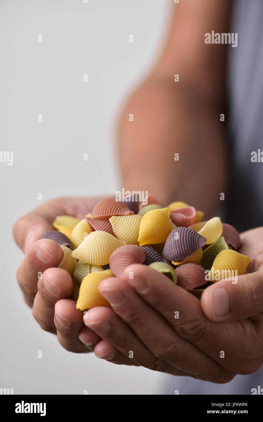 young man with a pile of uncooked conchiglie, italian seashell pasta ...