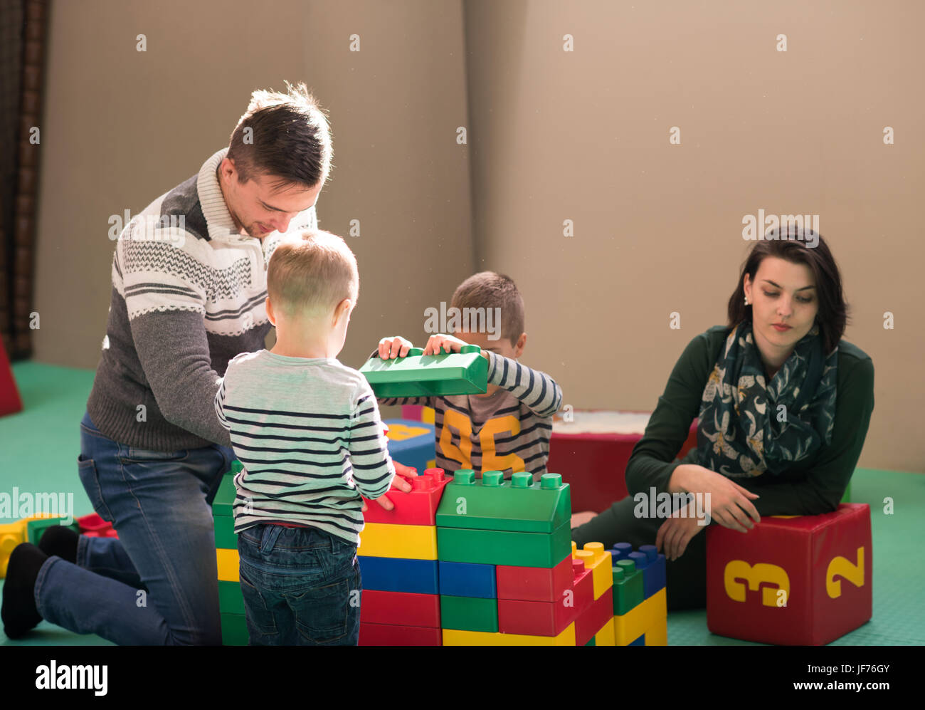 young happy parents having fun with kids in children playground indoor ...