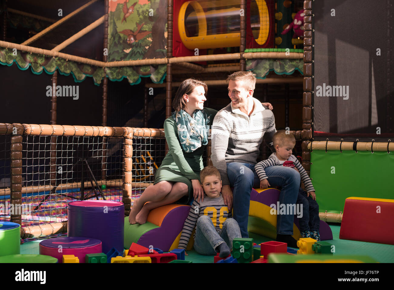 young happy parents having fun with kids in children playground indoor ...