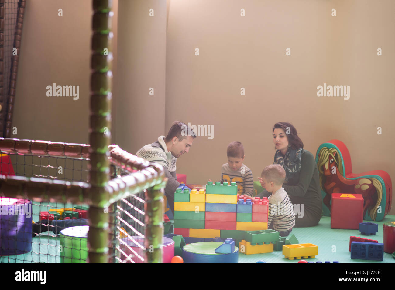 young happy parents having fun with kids in children playground indoor ...