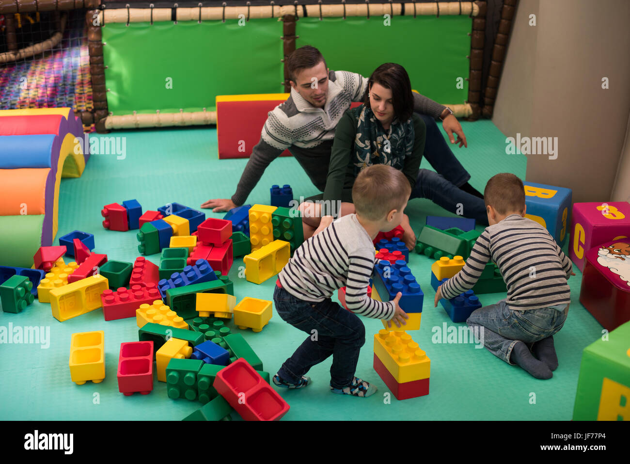 young happy parents having fun with kids in children playground indoor ...