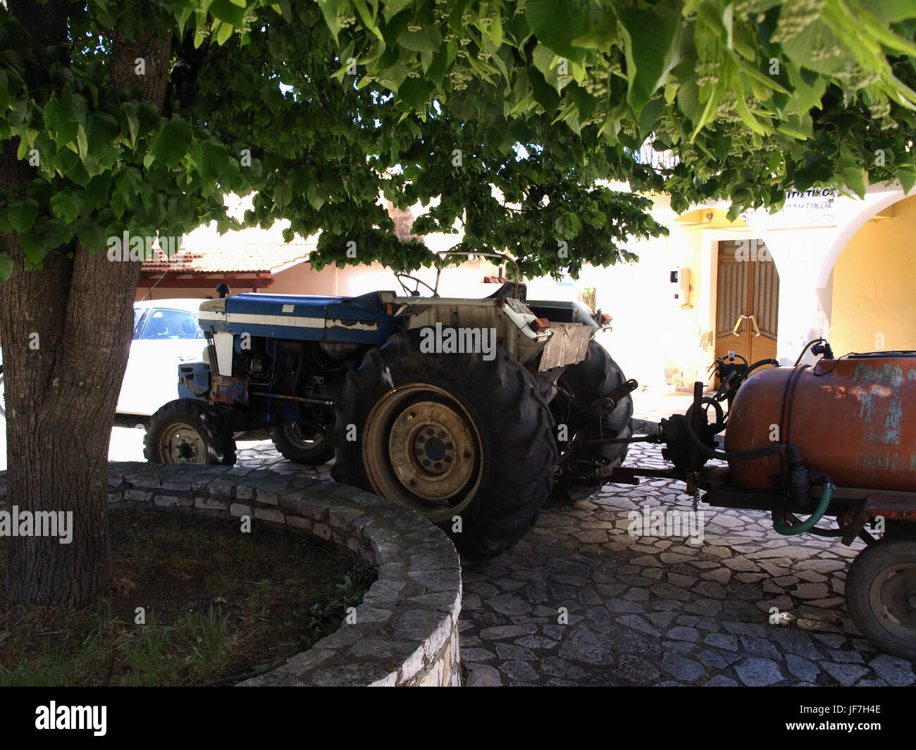 Old tractor parked in shade under tree in village square in Xanthates ...