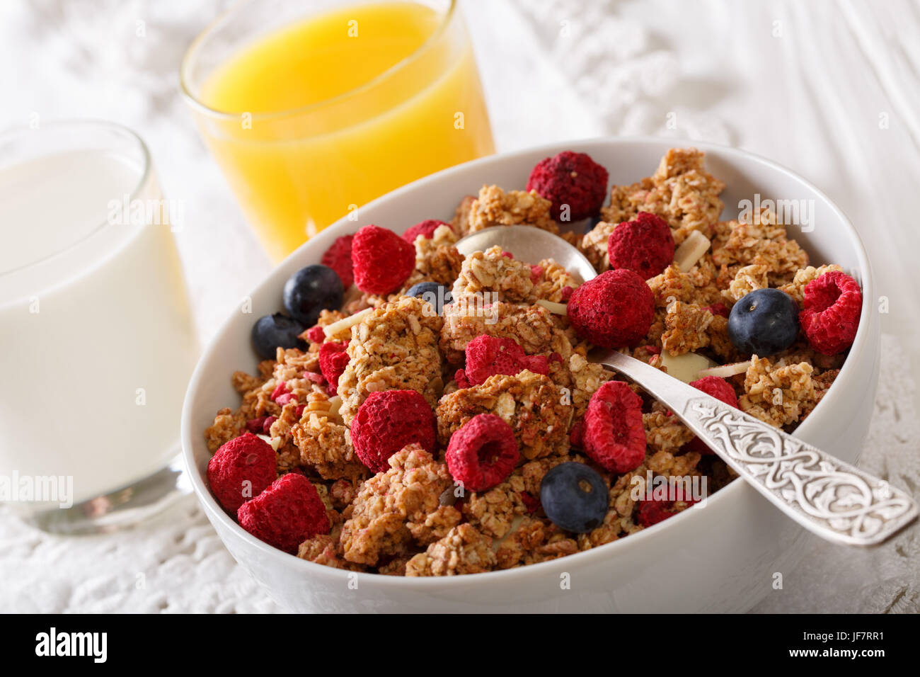Granola with raspberries and blueberries, milk and orange juice close ...