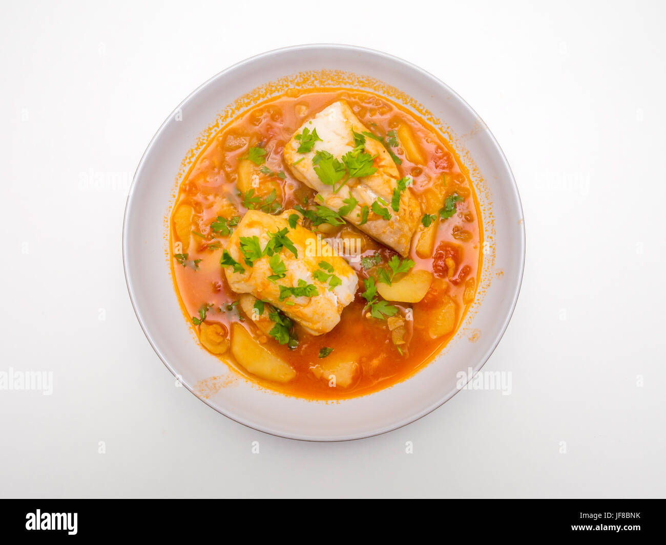 A bowl of fish stew with a two fillets of haddock on top dressed with ...