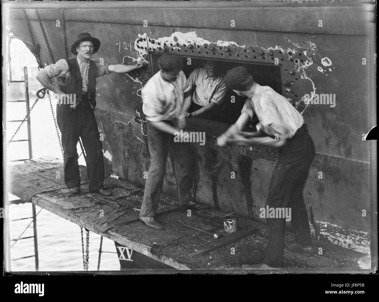 A historical image showing laborers working on the hull of a ship at ...