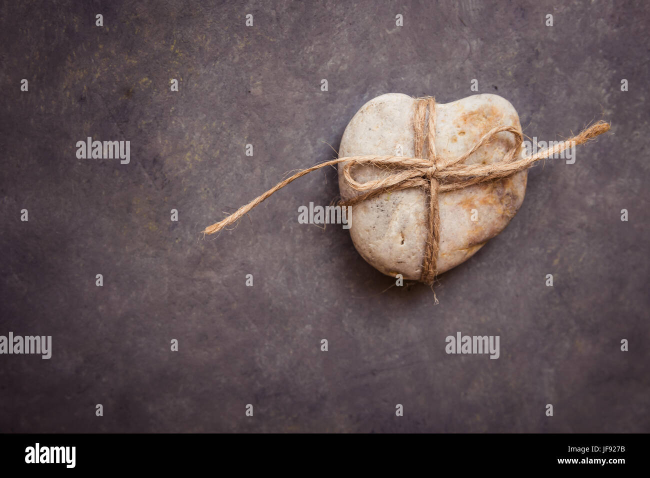 Heart shaped rock pebble tied with twine on dark blue purple stone ...