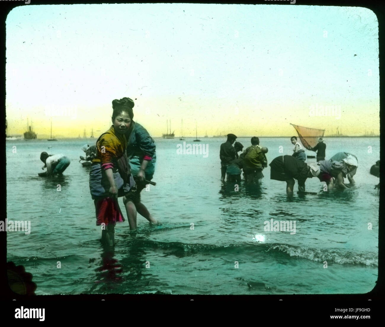People wading in sea; fisher with hand net; boats in historical image ...
