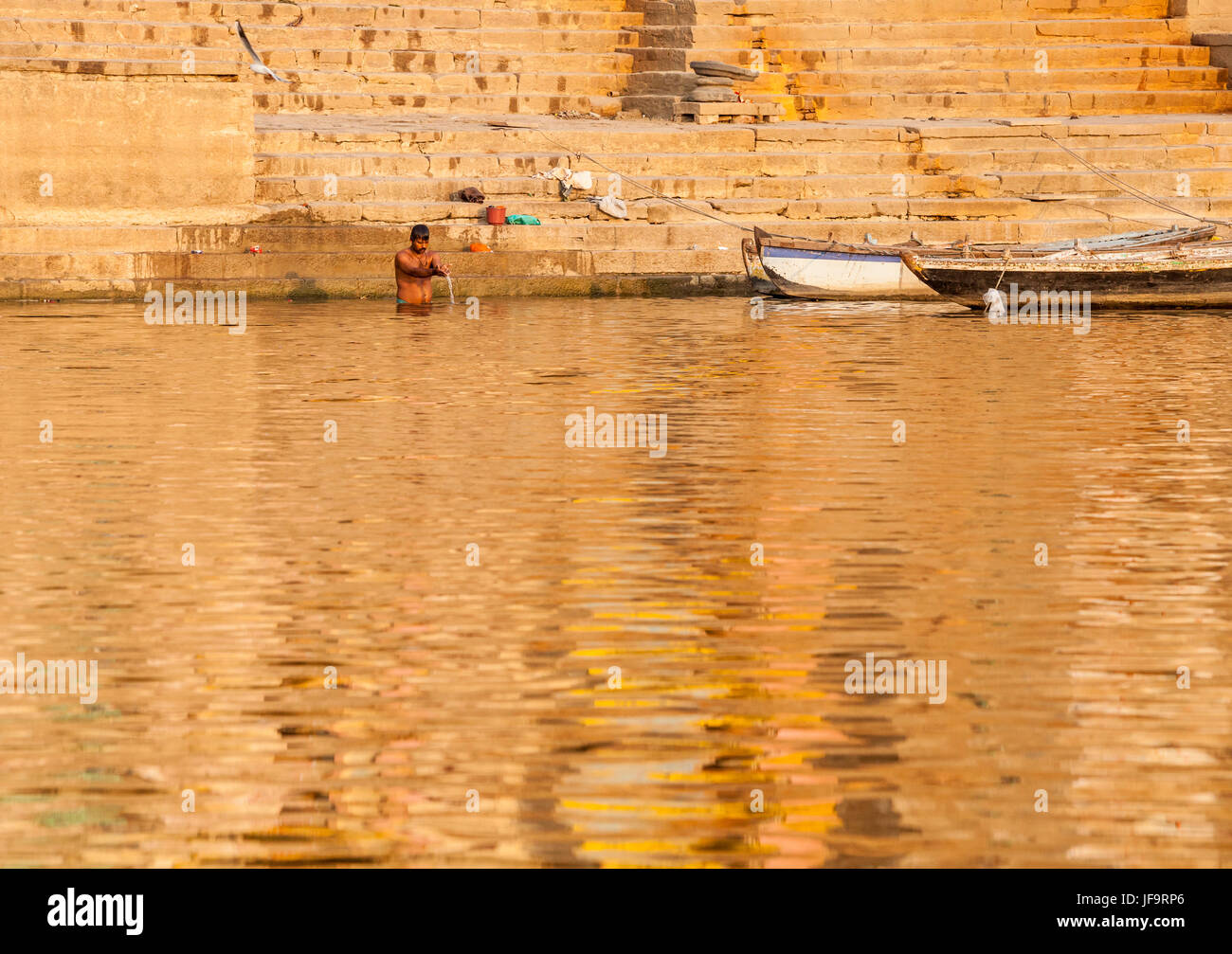 A man bathing in the waters of the Ganges river below a ghat in ...