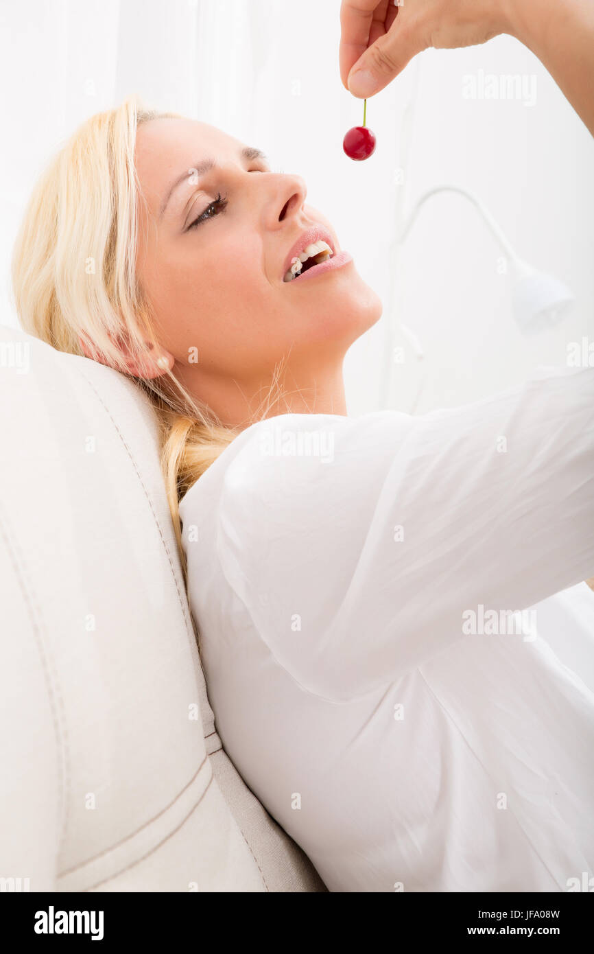 Woman eating cherry on the sofa Stock Photo - Alamy