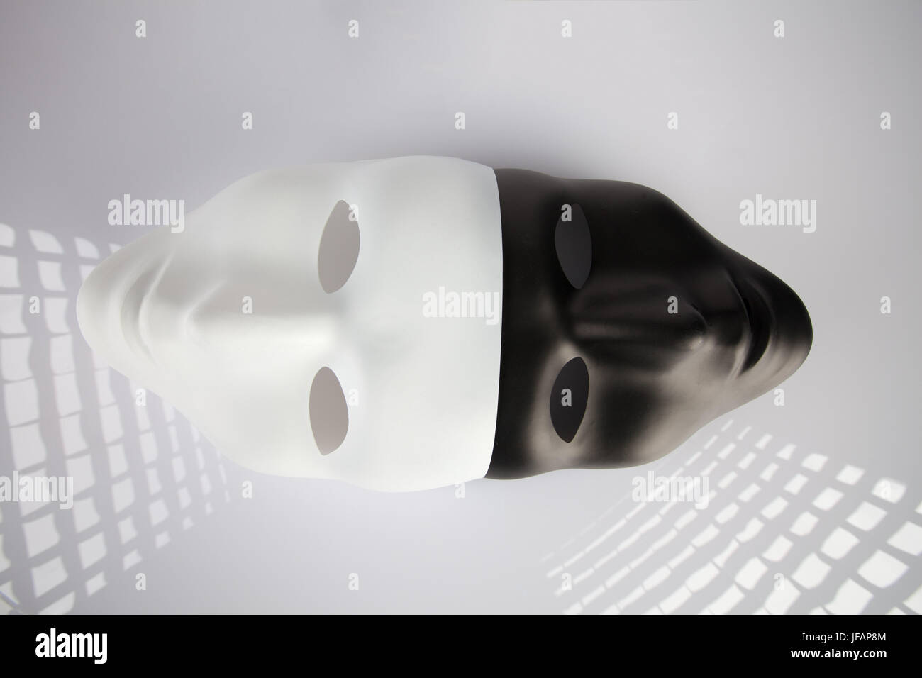 Black and white masks joined on white reflective background, top view ...