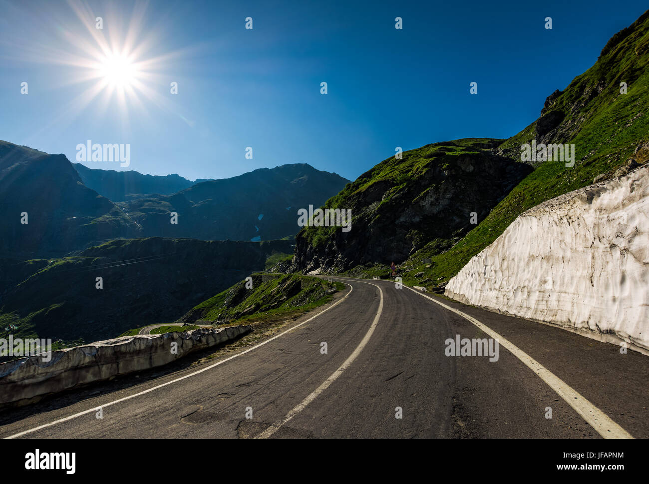 asphalt road uphill through mountain range. snow and grass on hillside ...