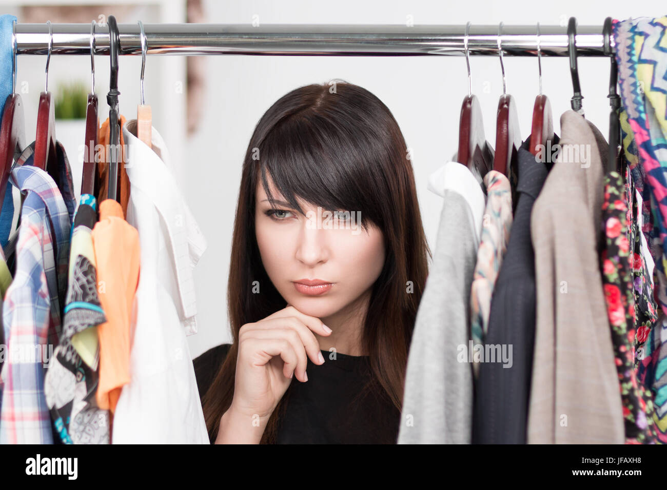Beautiful young confused woman near rack with clothes. Nothing to wear ...