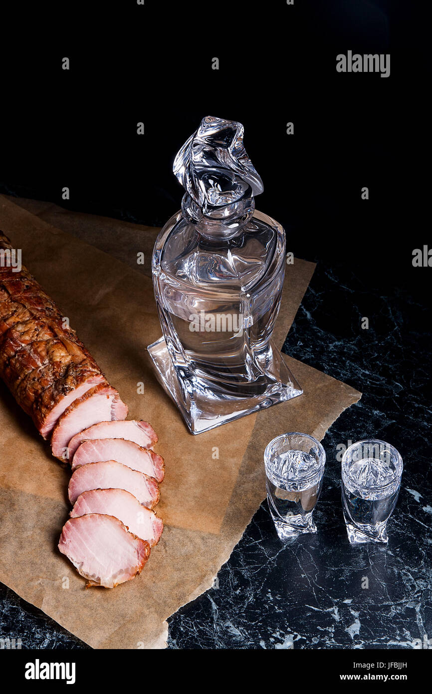 Bottle and shot glasses with vodka. Slices of smoked meat or ham on ...