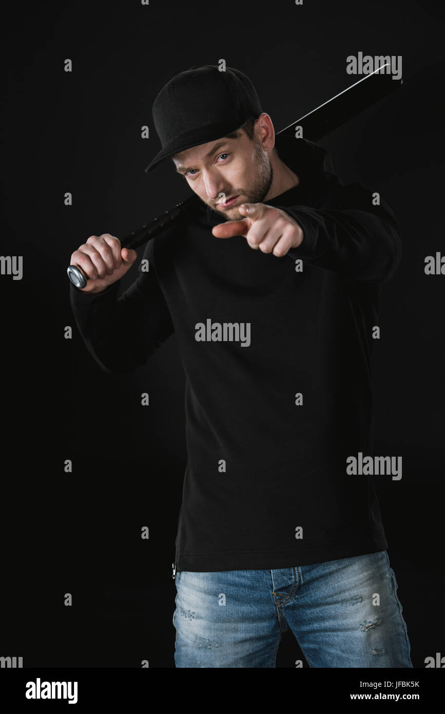 young robber in zoodie and cap with baseball bat isolated on black ...