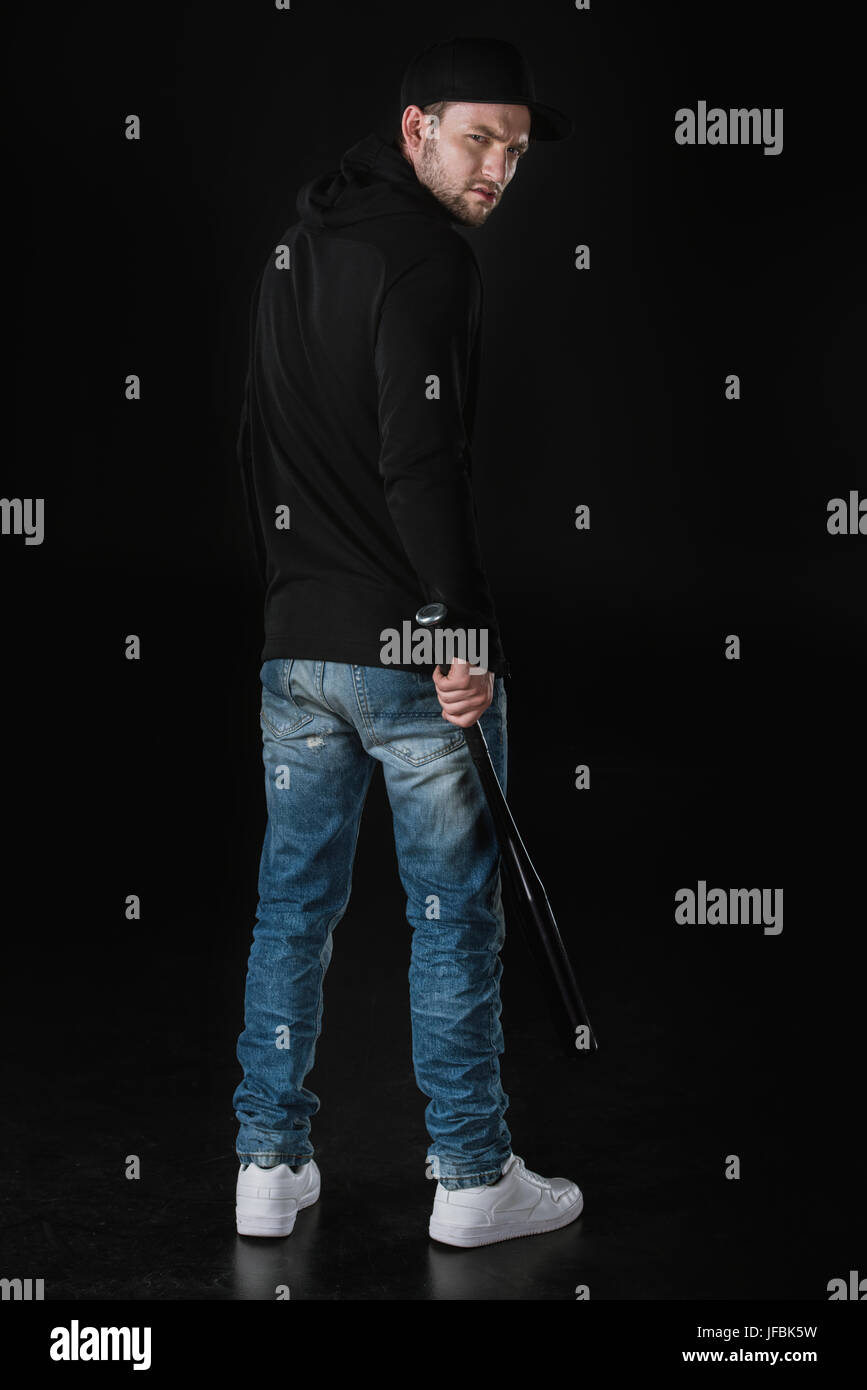young robber in zoodie and cap with baseball bat isolated on black ...