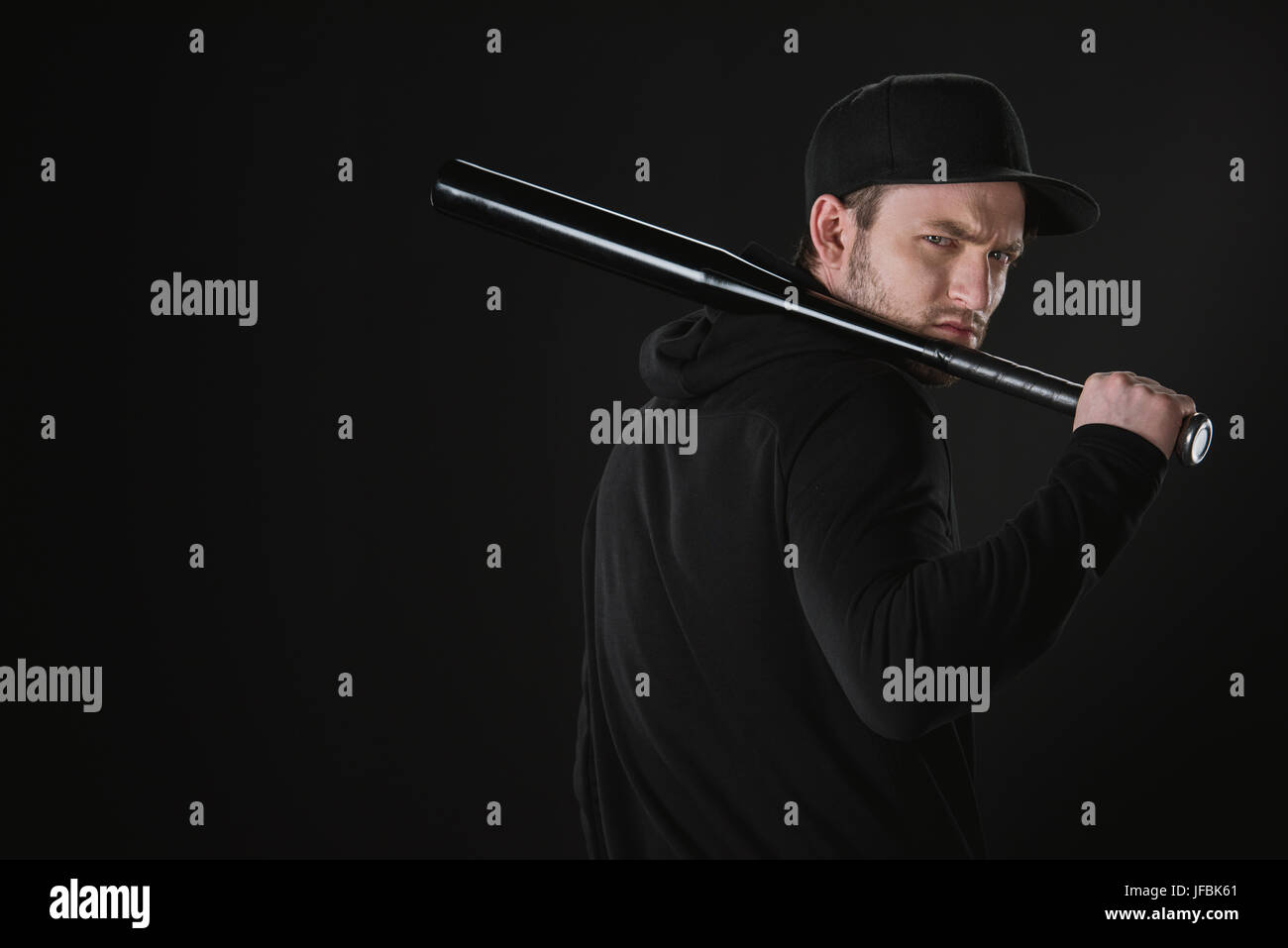 young robber in zoodie and cap with baseball bat isolated on black ...