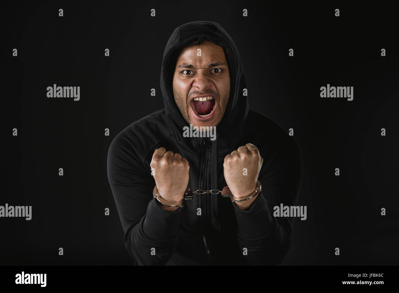young african american robber in zoodie and manacles isolated on black ...