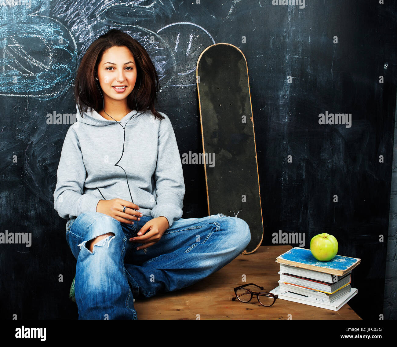 young cute teenage girl in classroom at blackboard seating on table ...